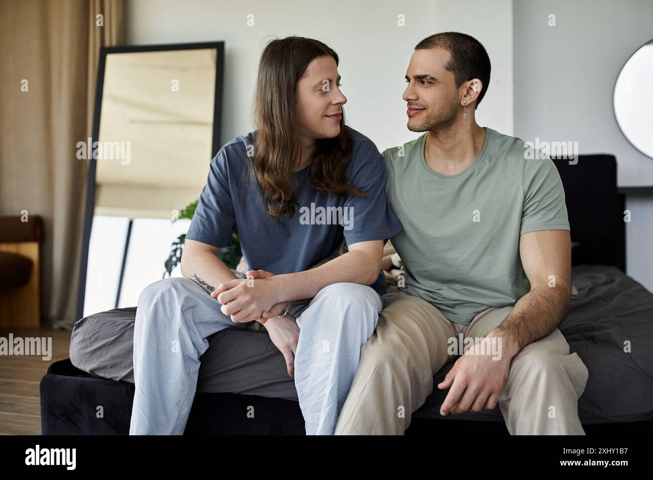 A young gay couple shares a tender moment on their bed, their eyes ...