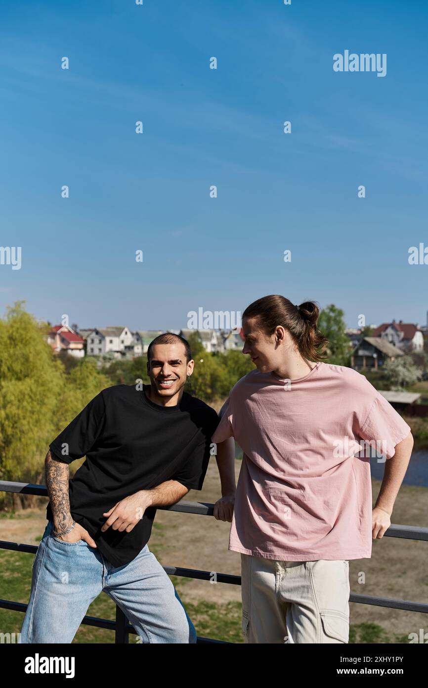 Two young men, dressed casually, stand side-by-side on a railing ...