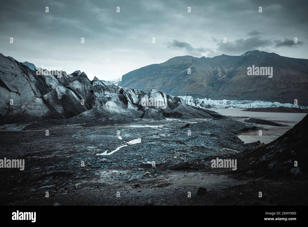 VATNAJOKULL Melting glacier ice creates a stream flowing through dark ...