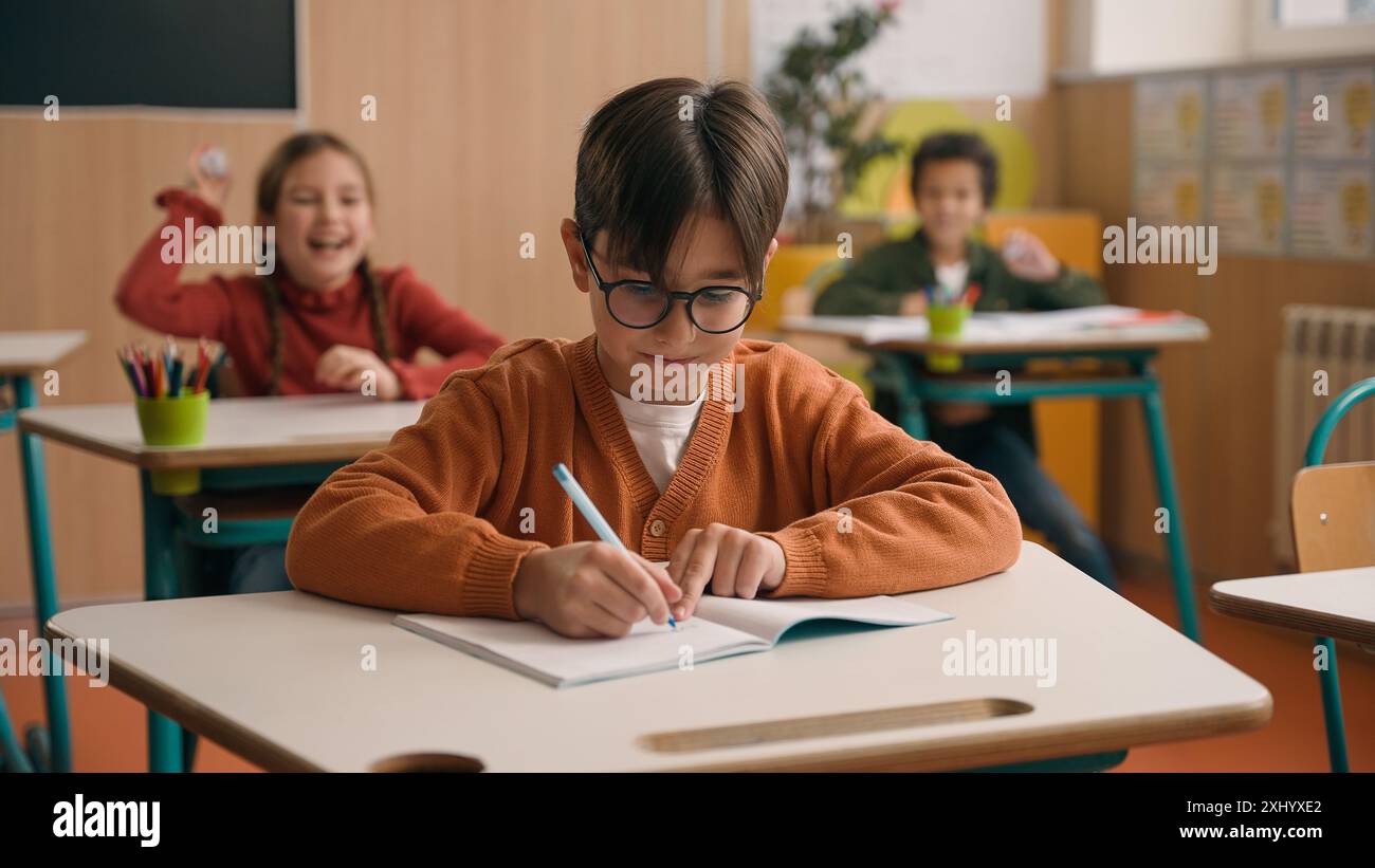 Caucasian little boy kid schoolboy nerd in glasses write task class ...