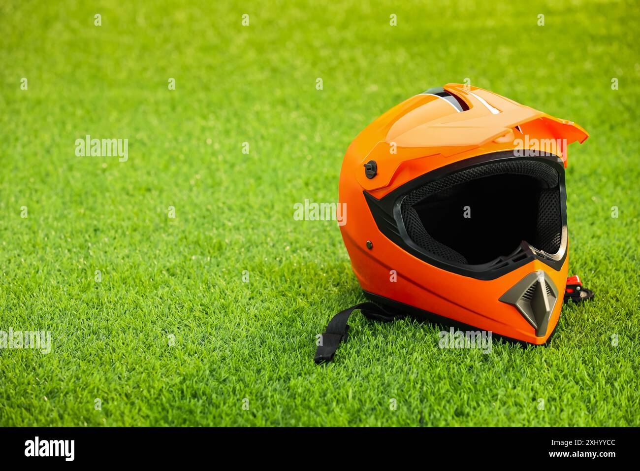 Orange motorcycle helmet with visor on green grass, space for text ...