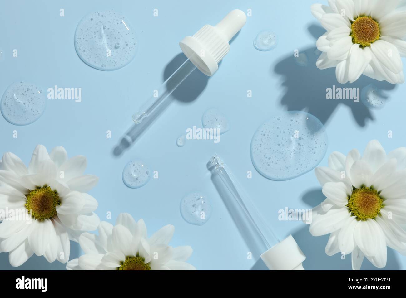 Beautiful daisy flowers, pipettes and drops of cosmetic serum on light ...