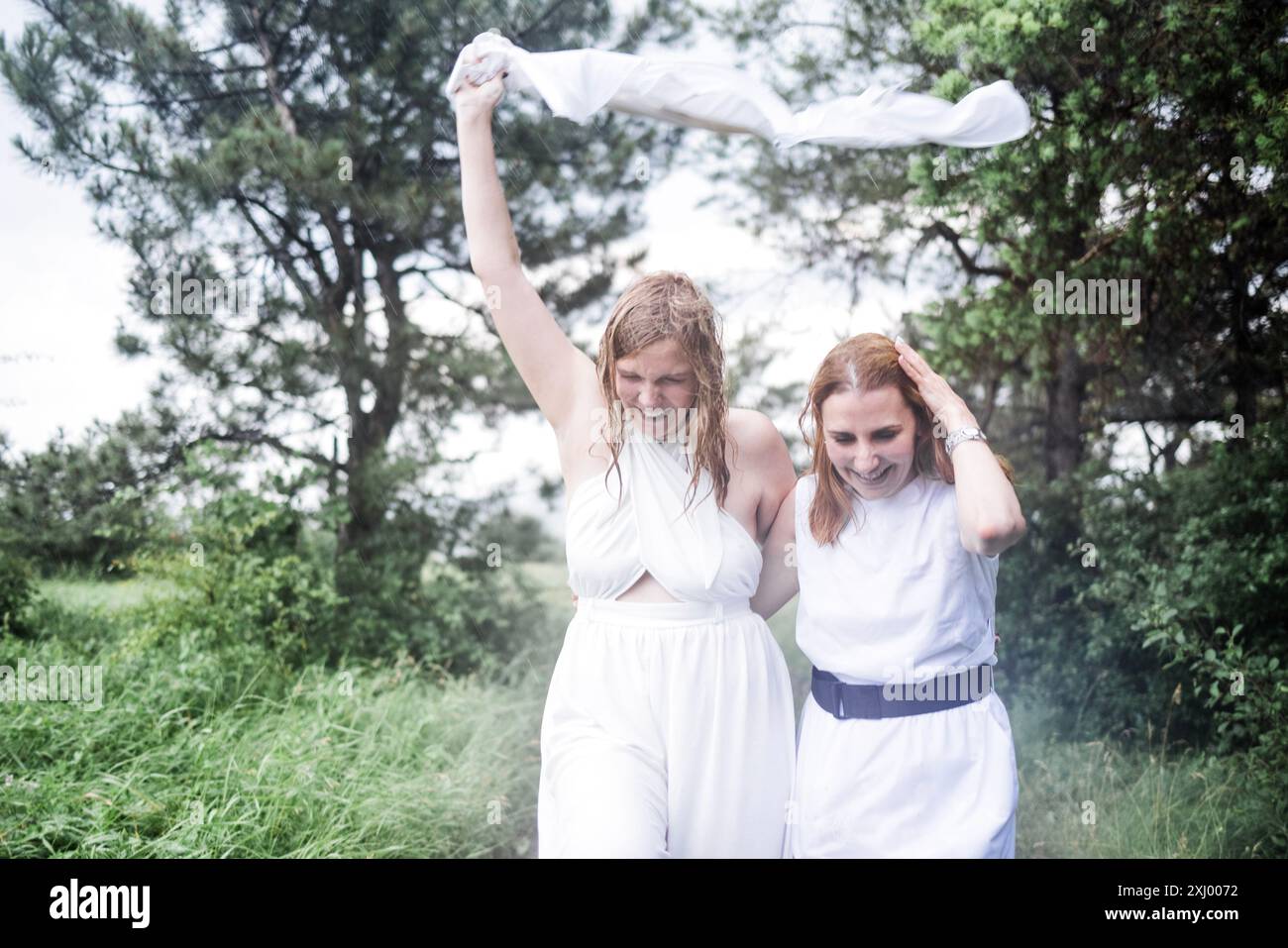 Two charming girls in white dresses are running in the summer rain. The ...