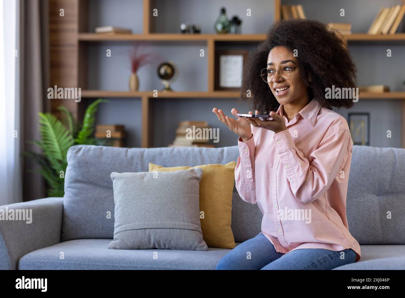 Woman sitting comfortably on couch using voice assistant on smartphone ...
