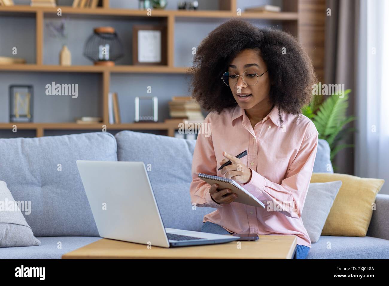 Woman working remotely from home on laptop, taking notes during online ...