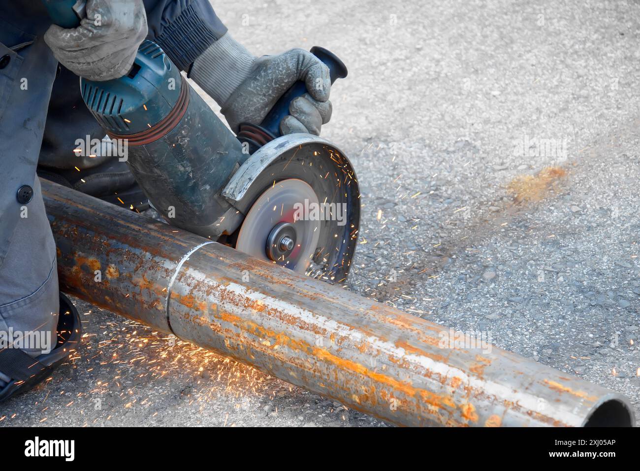A worker wearing knee pads is cutting a large metal pipe with an angle ...