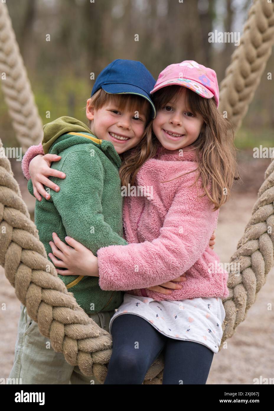 girl tenderly hugs her brother. Children sit on a swing in a city park ...