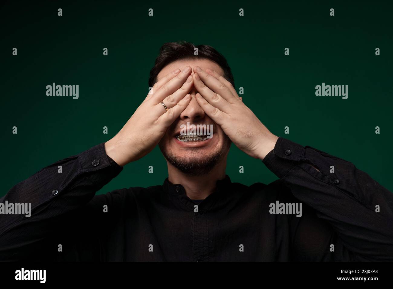 A man is seen with his hands covering his eyes in this image. He ...