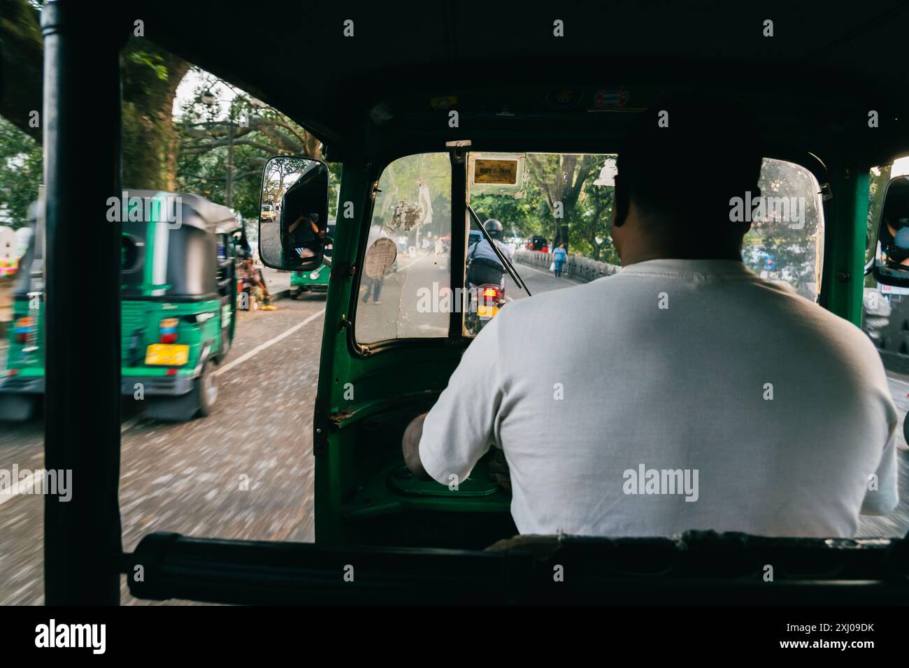Passenger seat view of a tuktuk driver driving along a busy main road ...
