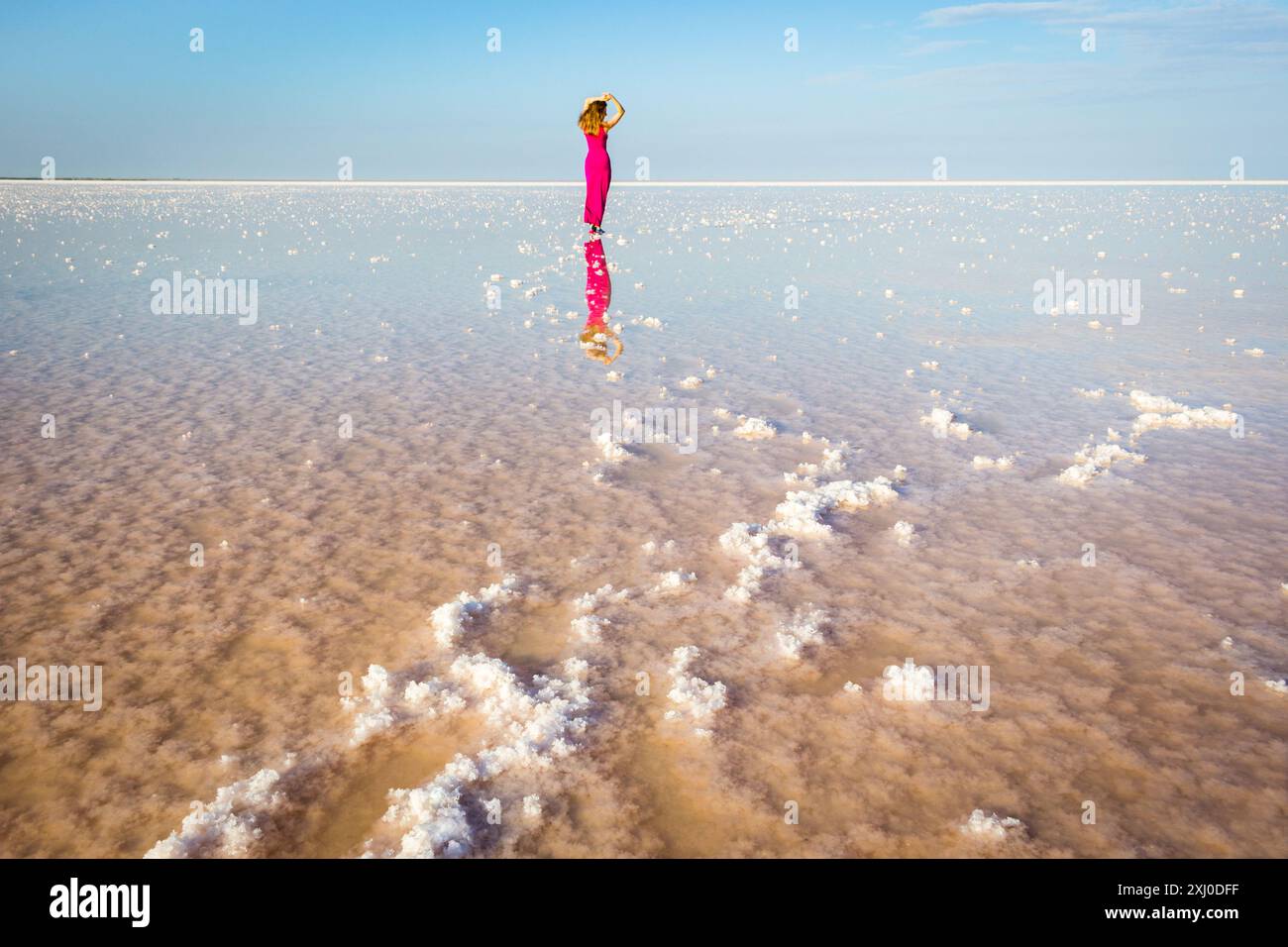 Young woman in red dress is staying on surface of salt lake with lumps ...