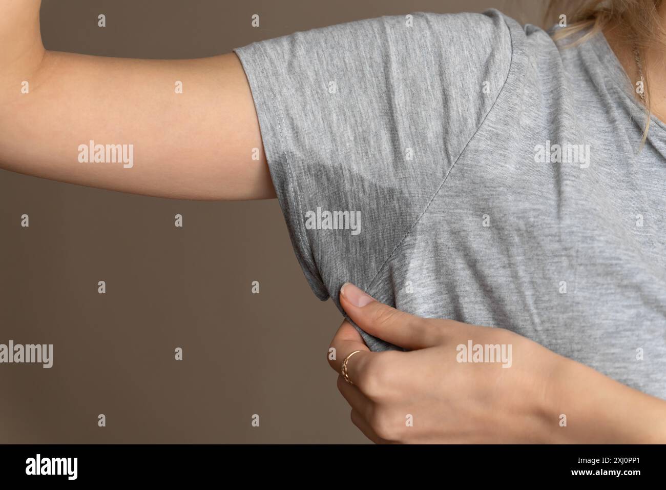 Close-up of a young woman shows a wet armpit on a gray T-shirt. Concept ...