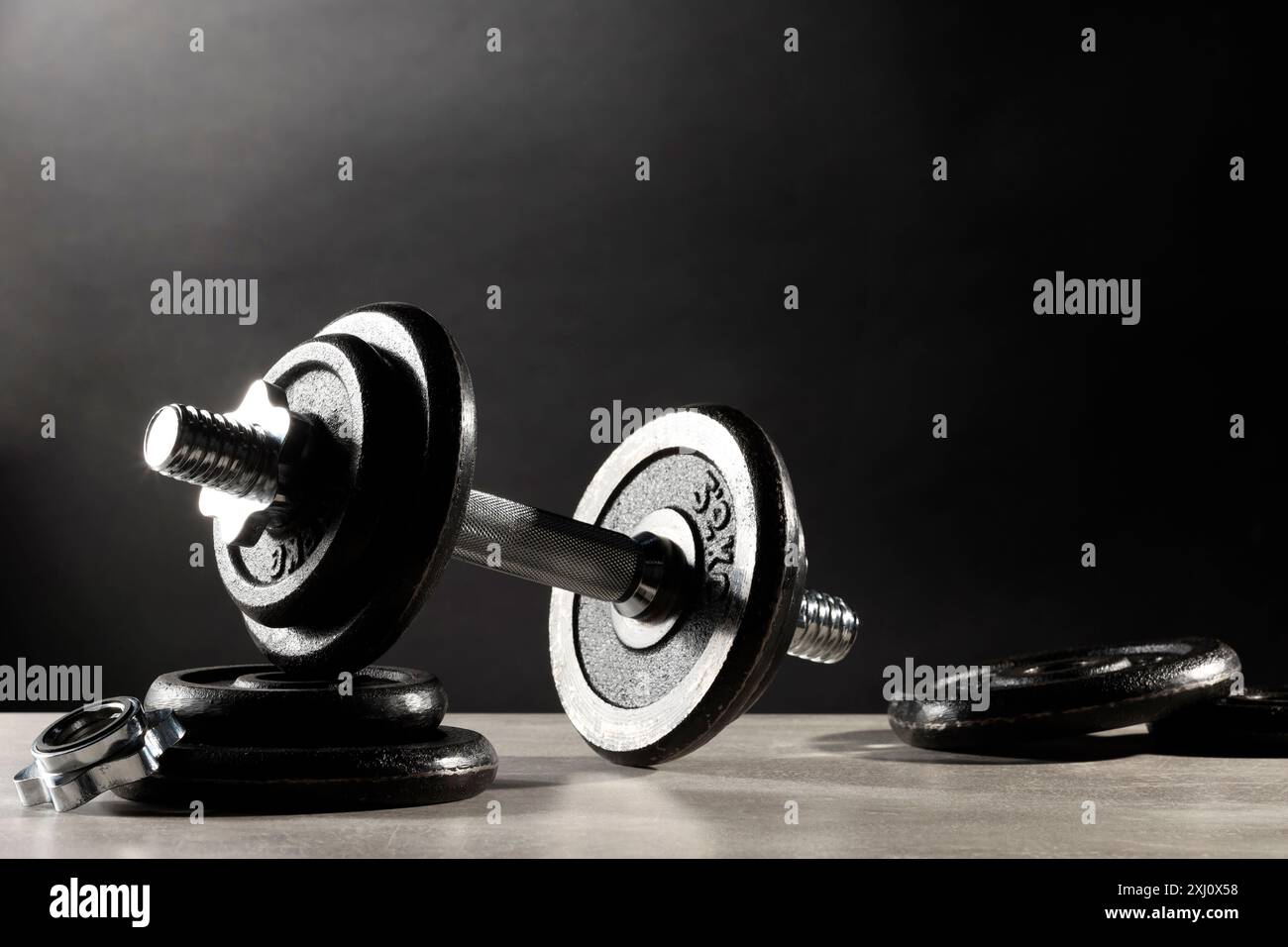Barbell and parts of one on light table against dark background Stock ...