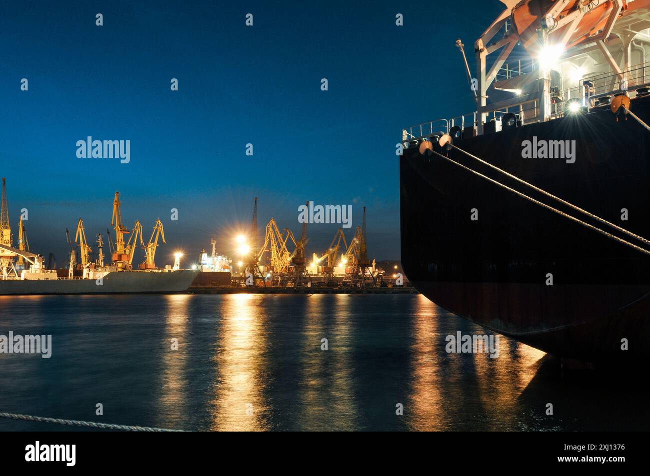 Night at the port. Cargo ship with black hull moored to the dock ...