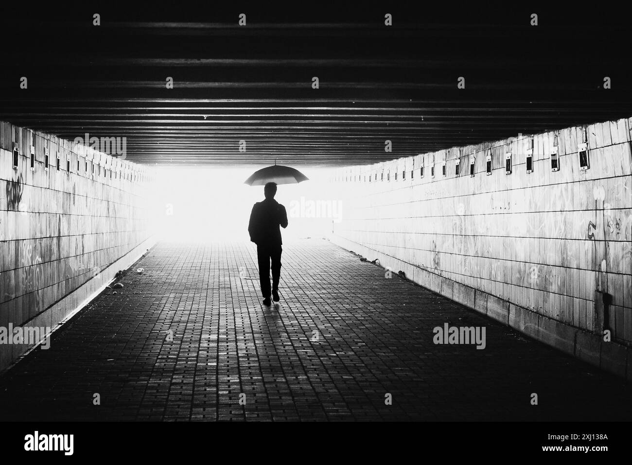 Silhouette of man with umbrella in a tunnel. Black and white image with ...