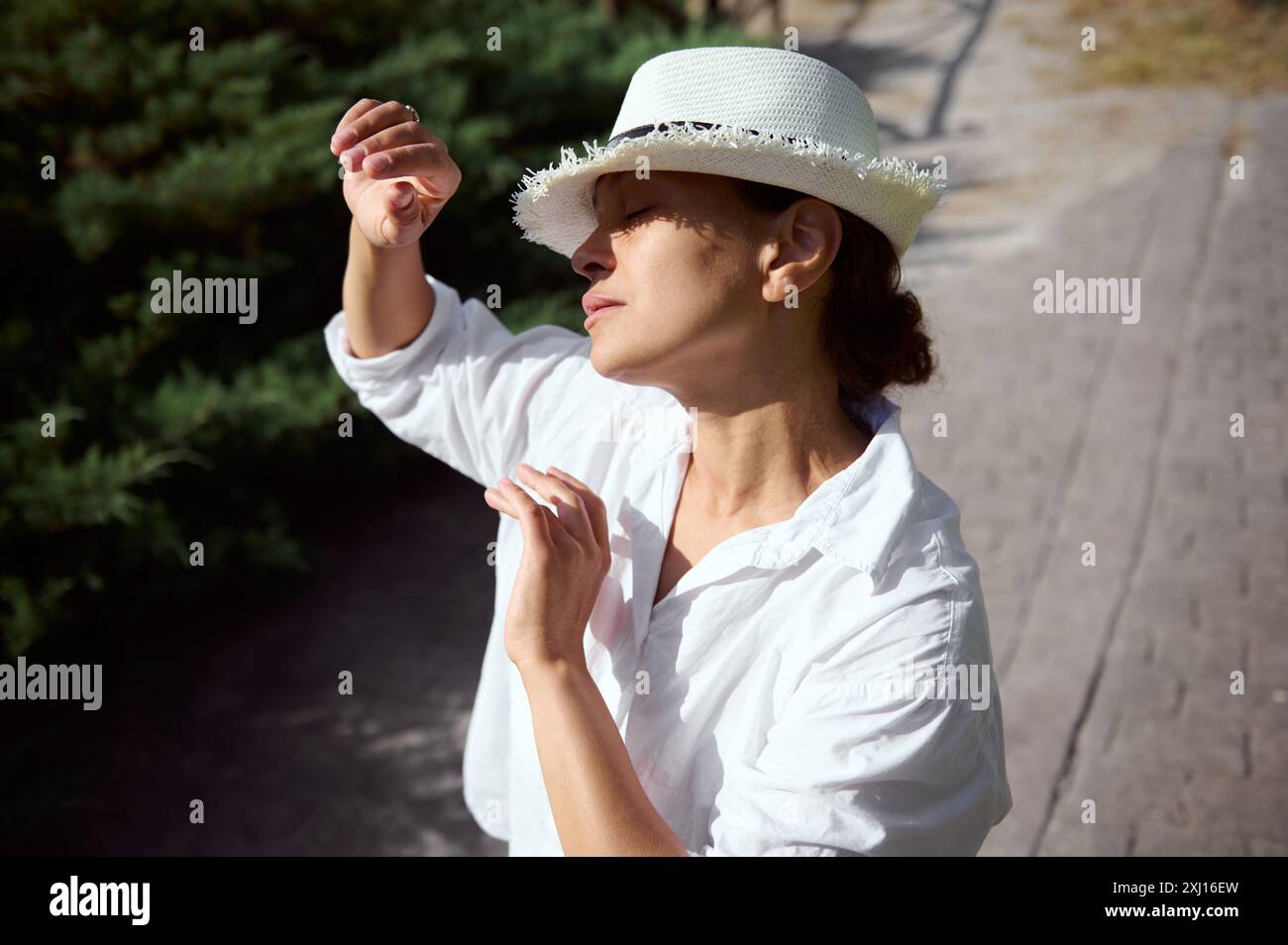 Middle-aged woman wearing a white hat and white shirt shielding her eyes from the bright ...