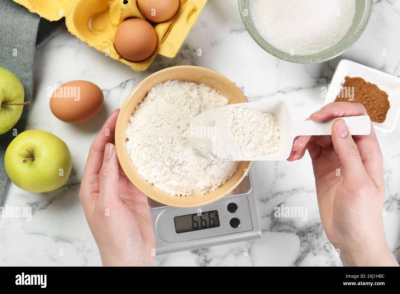 Woman adding flour into bowl on kitchen scale at white marble table ...