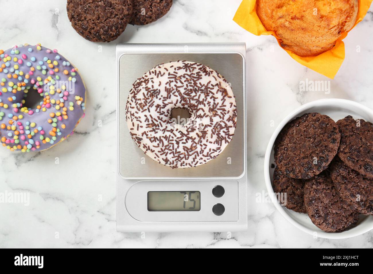Flat lay composition of kitchen scale with donut on white marble table ...