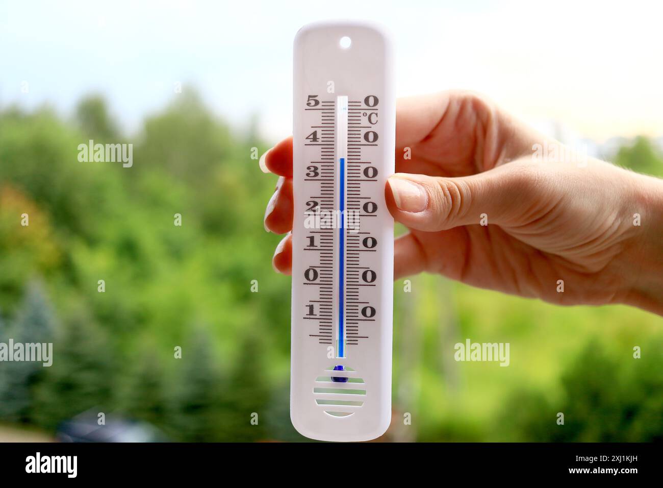 A womans hand with a plastic mercury thermometer shows high air ...