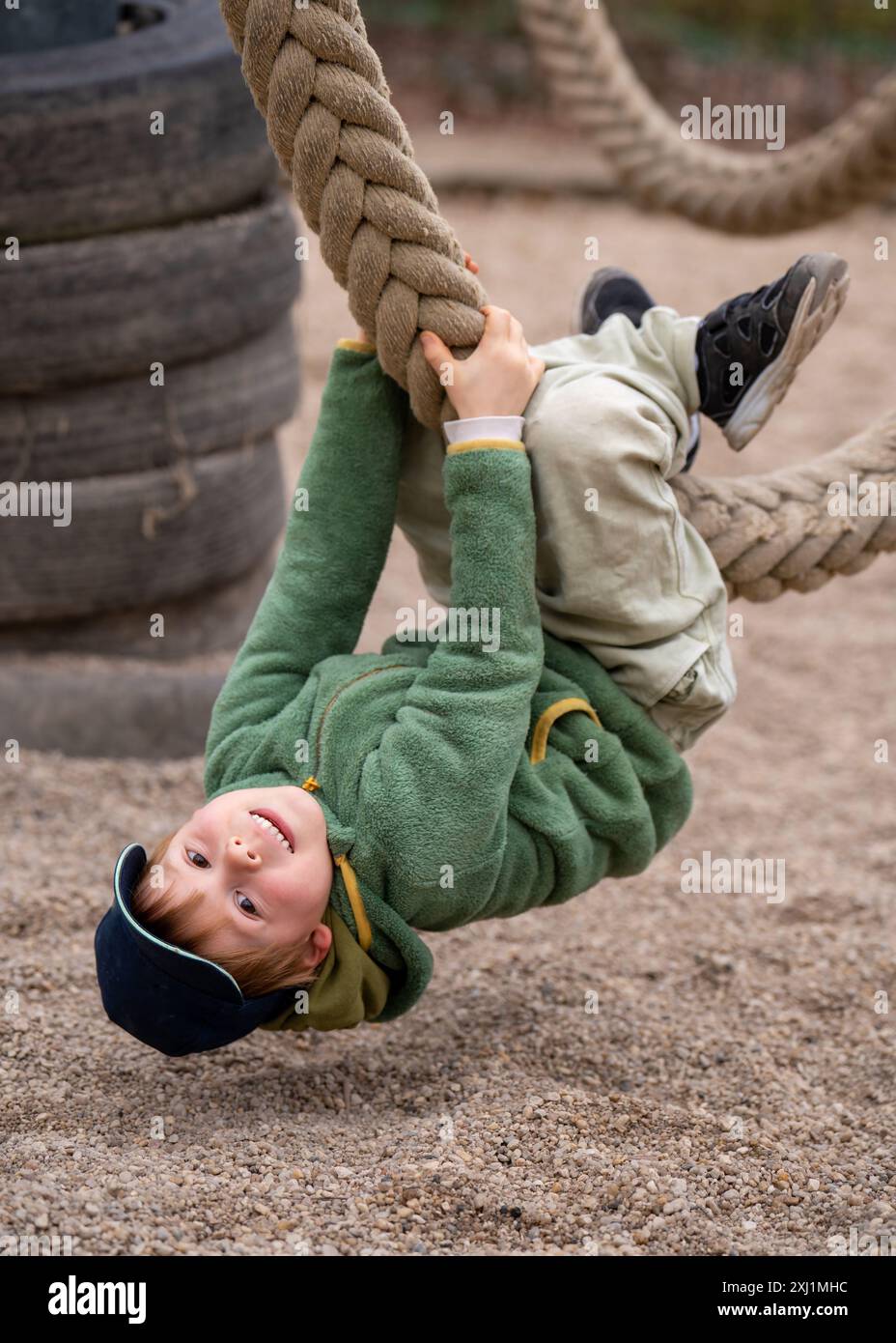A cheerful 5-year-old boy spends time outdoors. He frolics on a rope ...