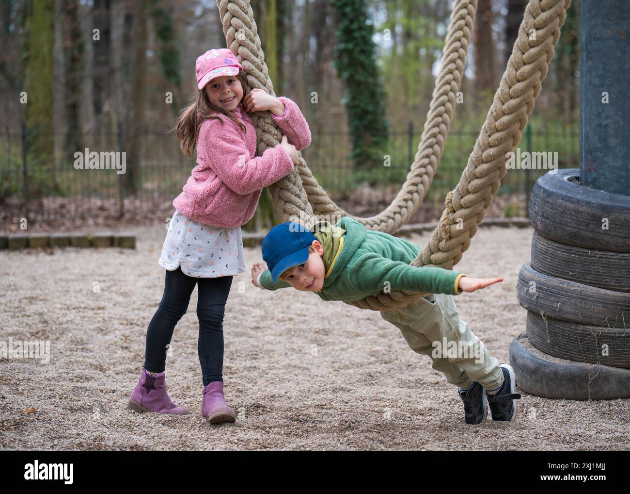 Cute children having fun outdoors. They ride on a swing. A girl stands ...