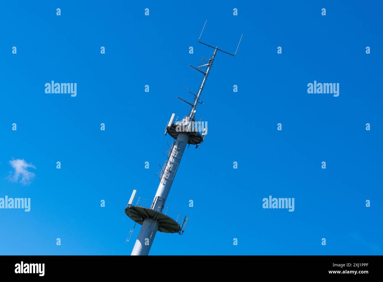 A tall telecommunication tower with multiple antennas stands against a clear blue sky with a ...
