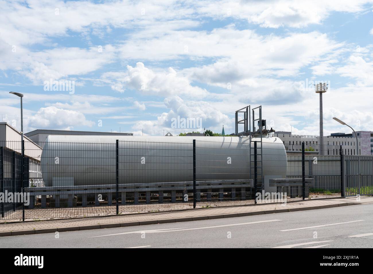 A large, cylindrical tank sits behind a chain-link fence, surrounded by ...