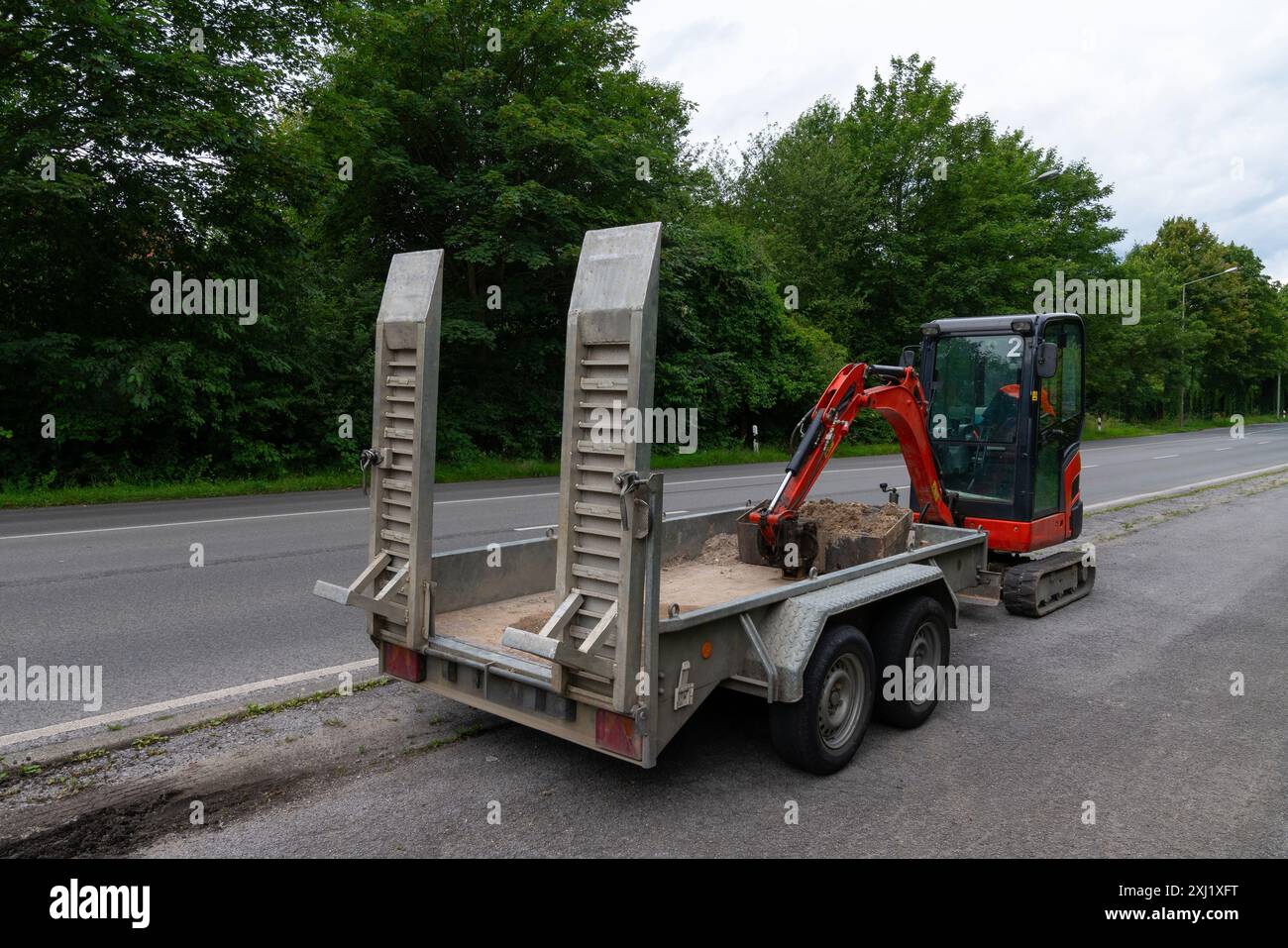 A red excavator is loaded onto a trailer on the side of a road, ready ...