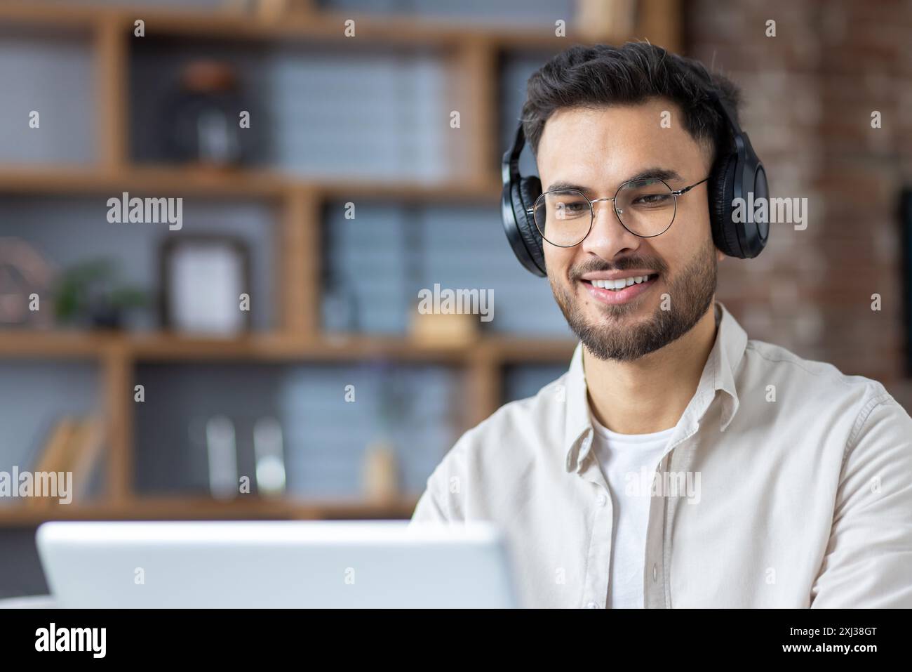Smiling young Muslim man working and studying remotely at home. He sits ...
