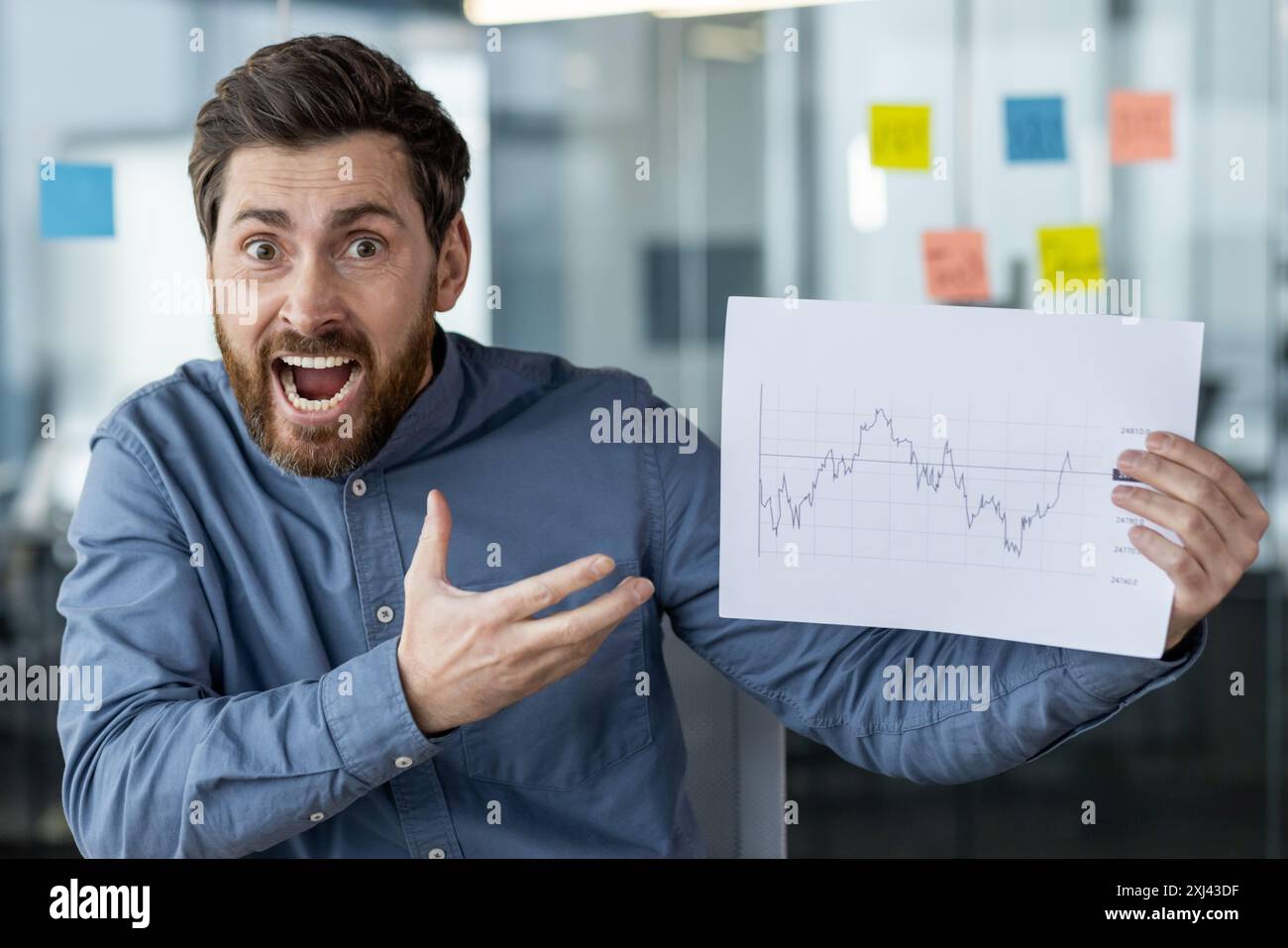 An angry young man sits in the office at the desk and emotionally shows ...