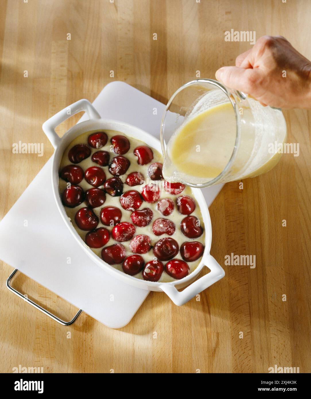 Pouring the almond mixture on the cherries in the clafoutis dish Stock ...