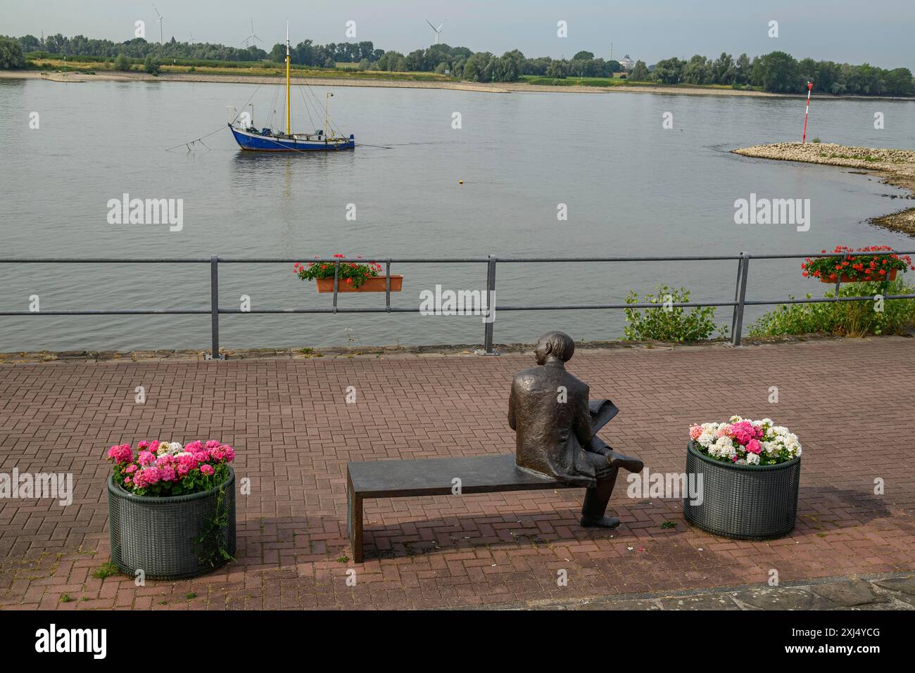 A statue on a bench with a view of the river and a boat in the water ...