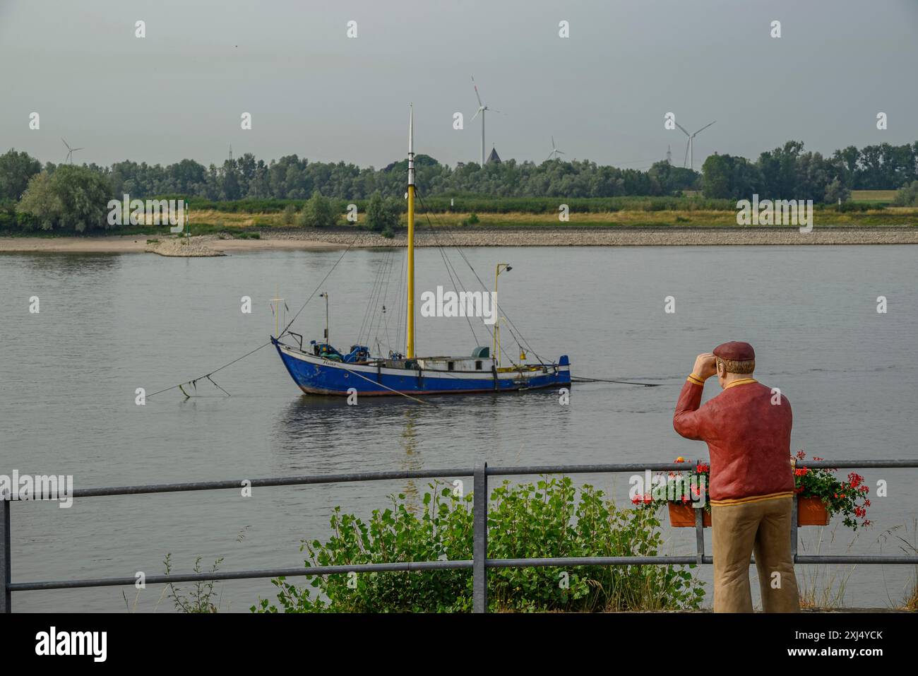 A statue looks at a boat in the river, windmills in the background ...