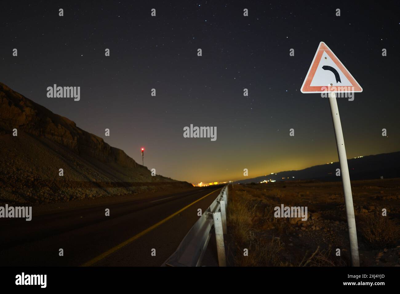 road sign indicating a left curve is illuminated under a starry night ...