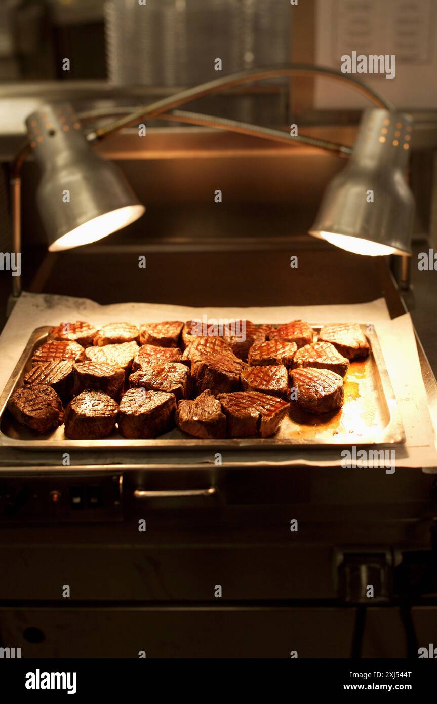 Thick beef steaks keeping warm under lights in a restaurant Stock Photo ...