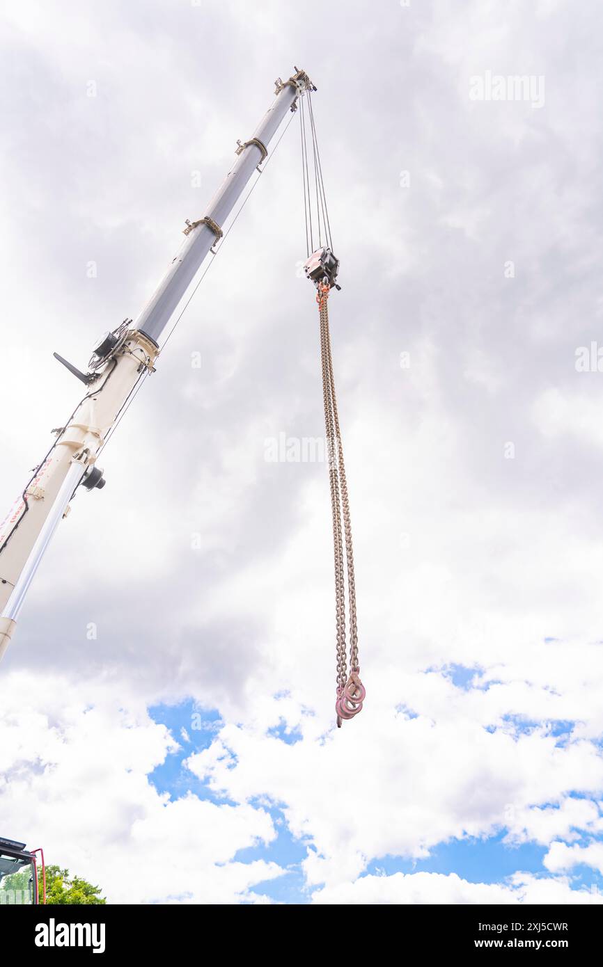 A high crane with a long hook and chains in front of a cloudy sky on a ...
