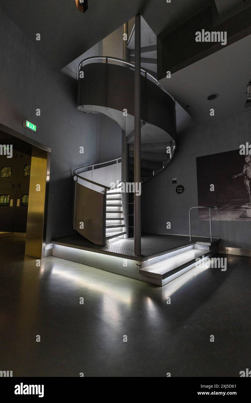 A modern spiral staircase made of metal, illuminated in a dark ...