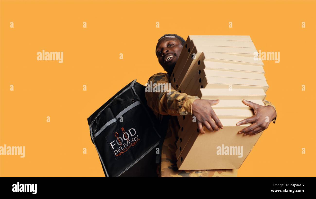 Young deliveryman giving huge stack of pizza boxes to client ...