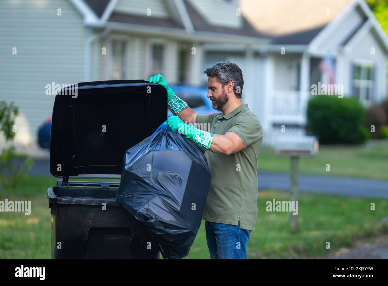 A man pushes a large plastic trash bin for weekly waste disposal ...