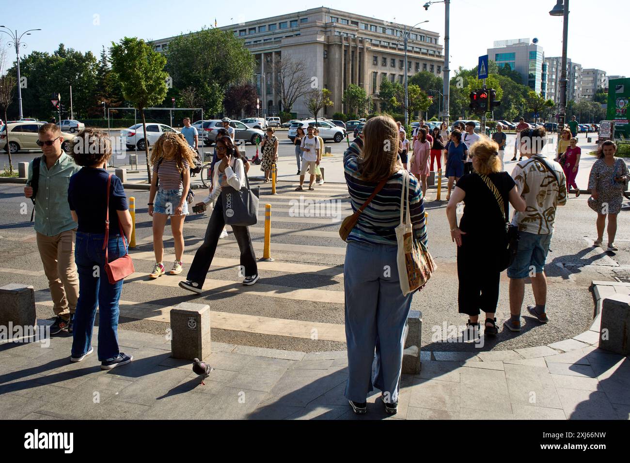 Bucharest, Romania - June 25, 2024: People cross the street near the Victoria Palace which ...
