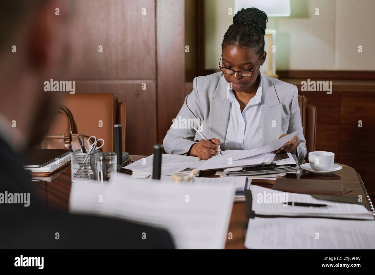 Young serious female notary in formalwear signing or certifying paper ...
