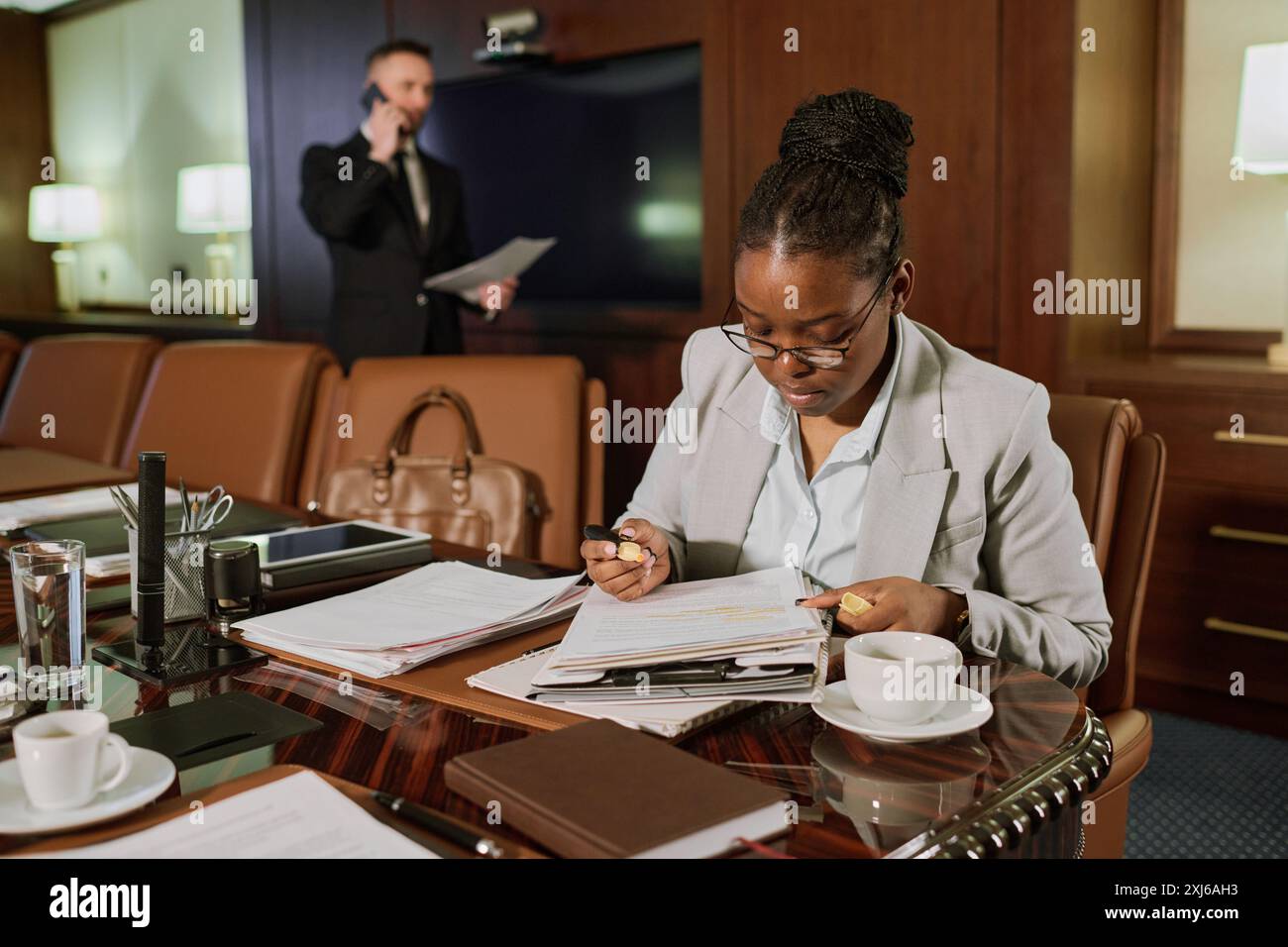 Serious young female solicitor bending over folder and paper documents ...