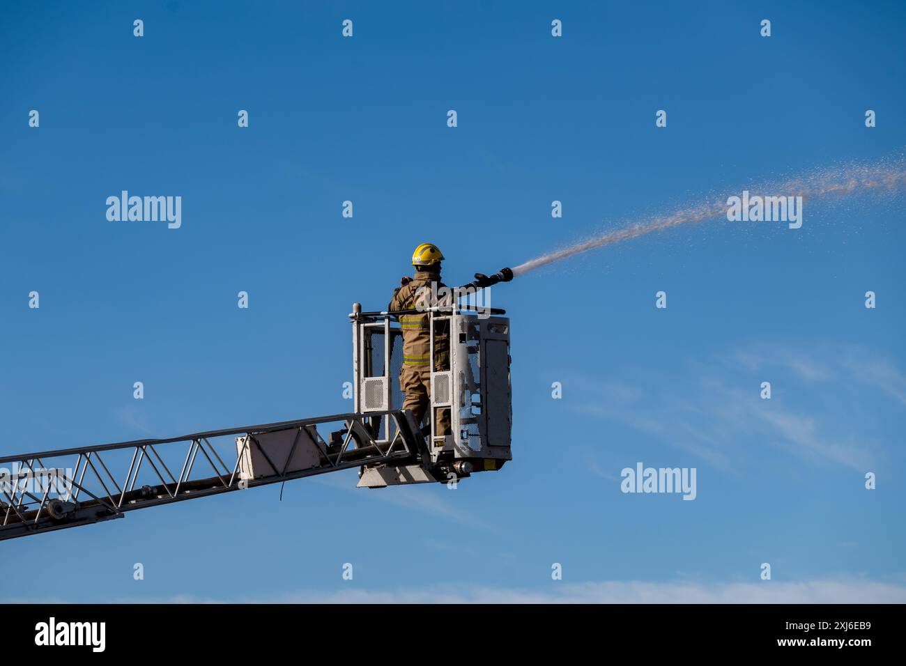 A firefighter is spraying water from a hose while standing on a ladder ...