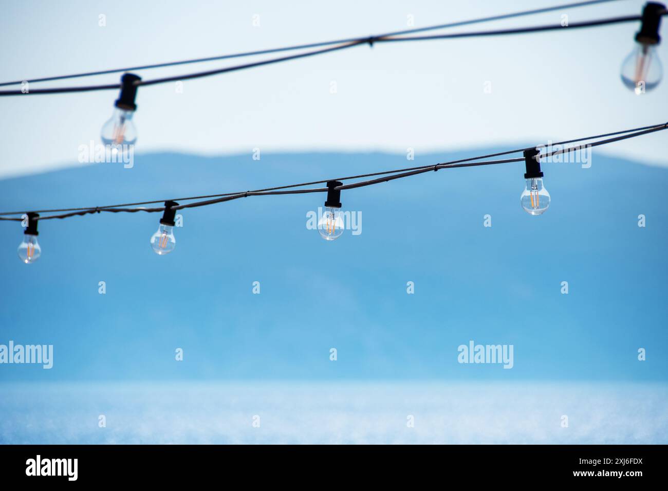 Clear Edison bulbs suspended on cables contrasting with a soft blue sky ...