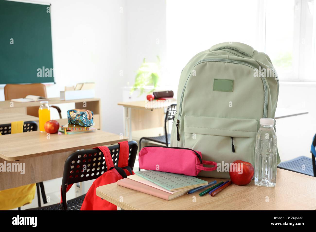 Backpack with apple, water bottle and pencil case on desk in classroom ...