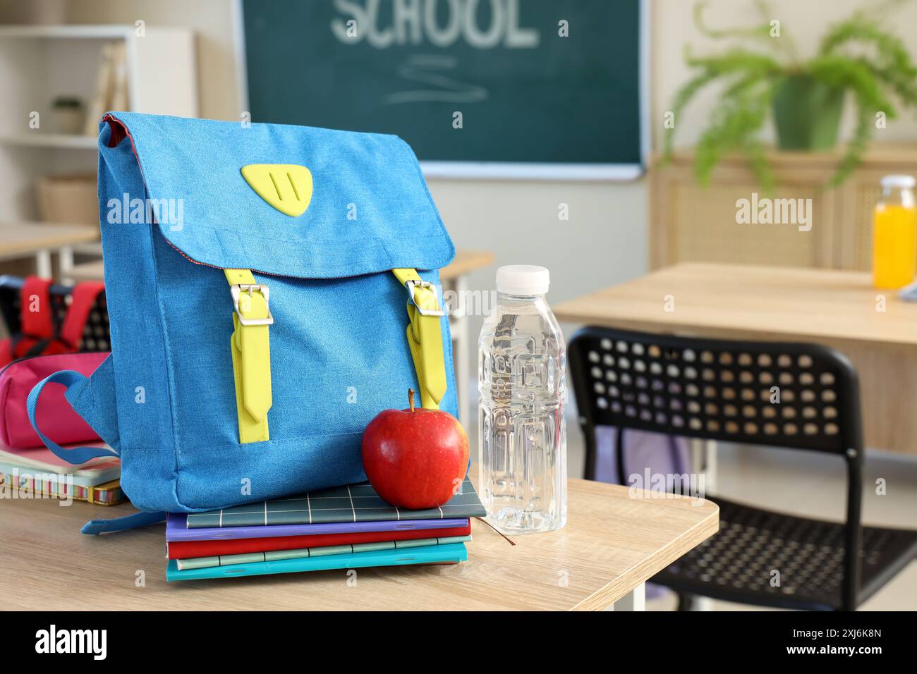 Blue backpack with apple, copybooks and water bottle on desk in ...