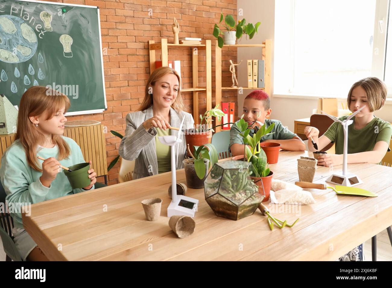 Female teacher and pupils planting during Ecology lesson in classroom ...