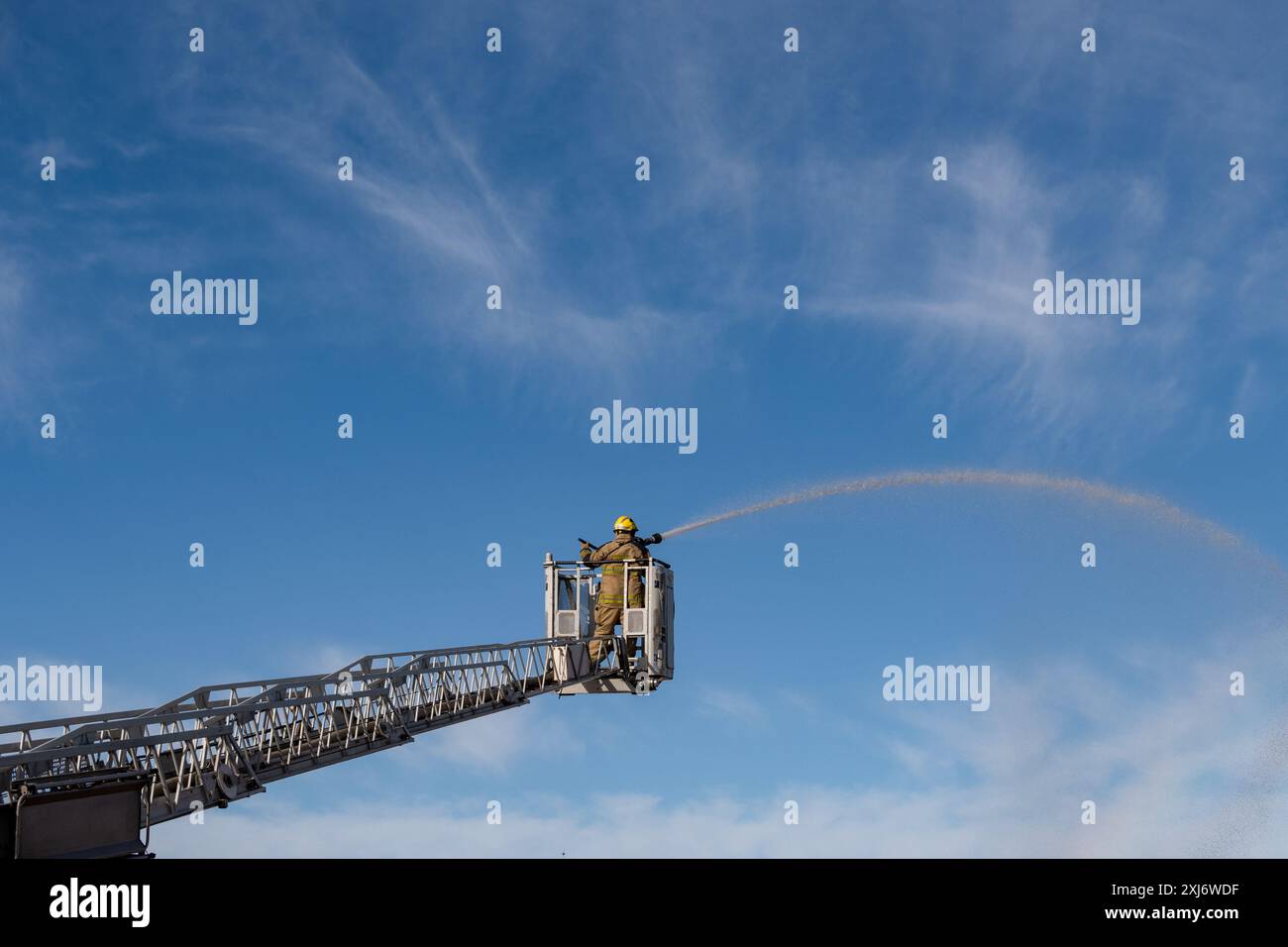 Firefighter on ladder, spraying water on fire, side view Stock Photo ...