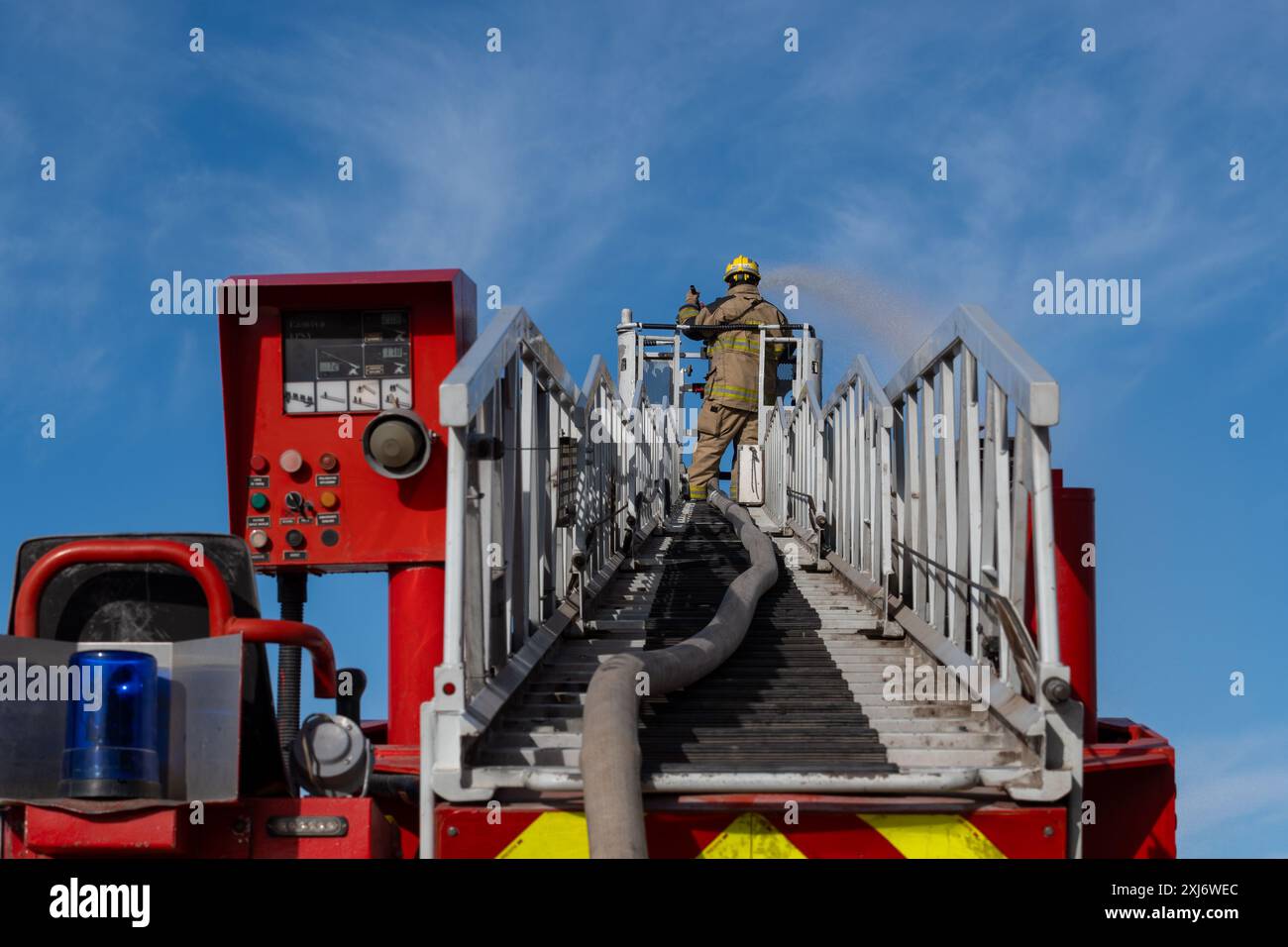 Firefighter on ladder, spraying water on fire, side view Stock Photo ...