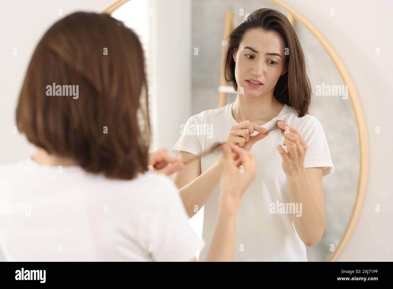 Stressed woman holding clump of lost hair near mirror indoors. Alopecia ...