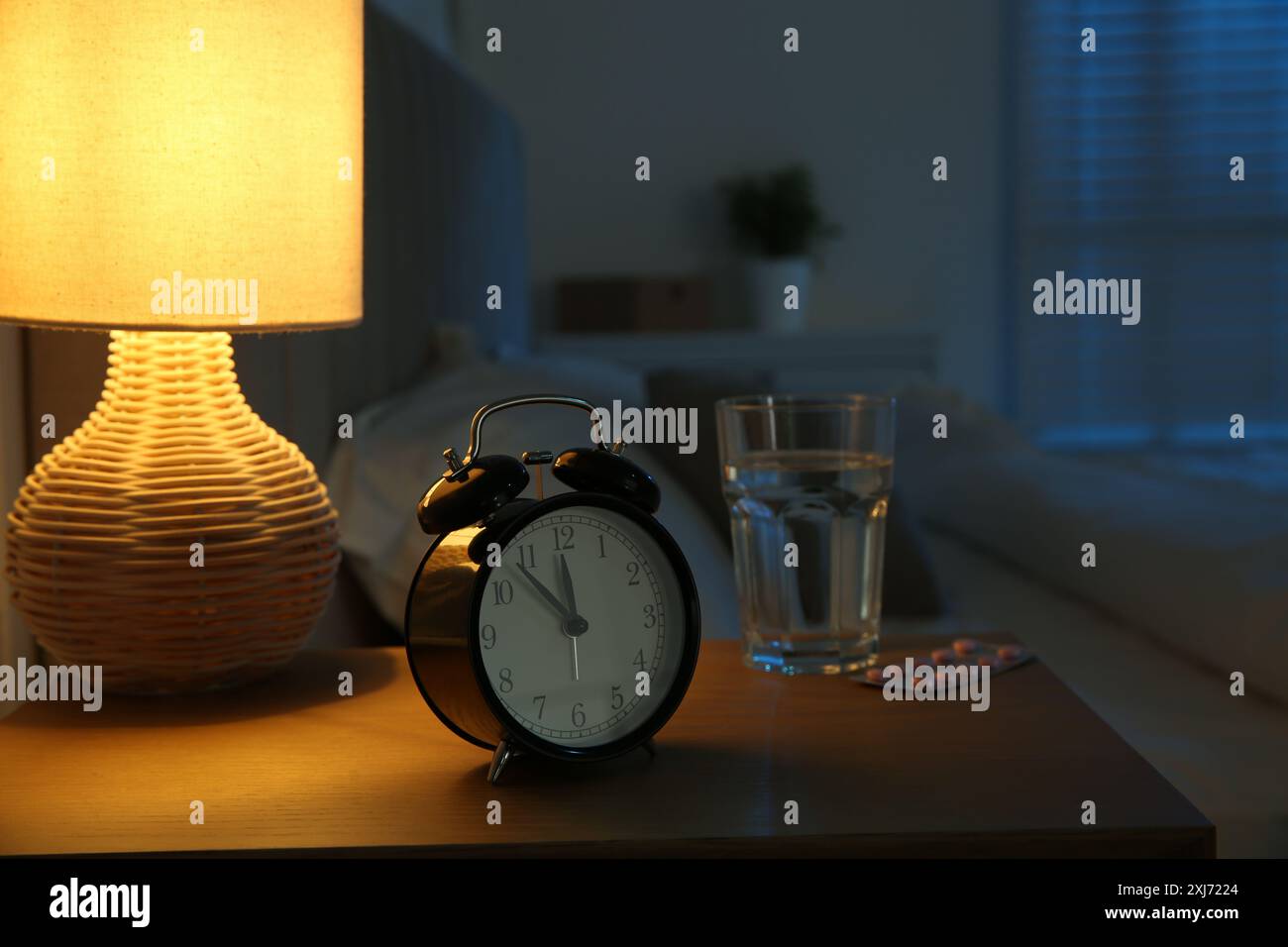 Insomnia treatment. Alarm clock, glass of water and pills on bedside ...